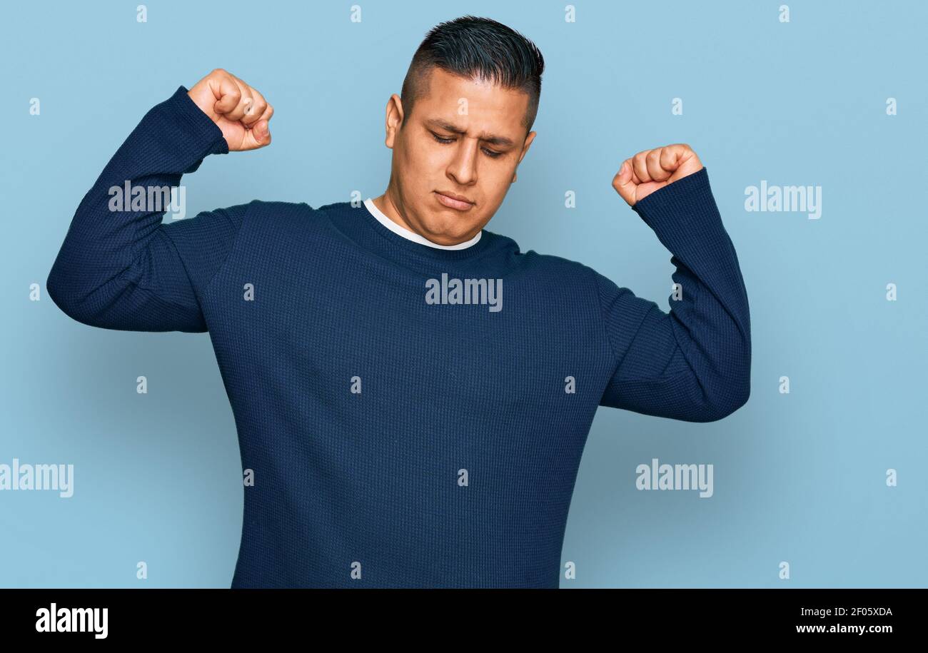 Young latin man wearing casual clothes showing arms muscles smiling ...