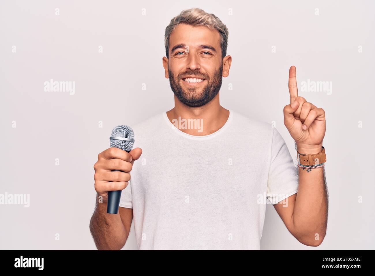 Handsome blond singer man with beard singing song using microphone over white background smiling ...