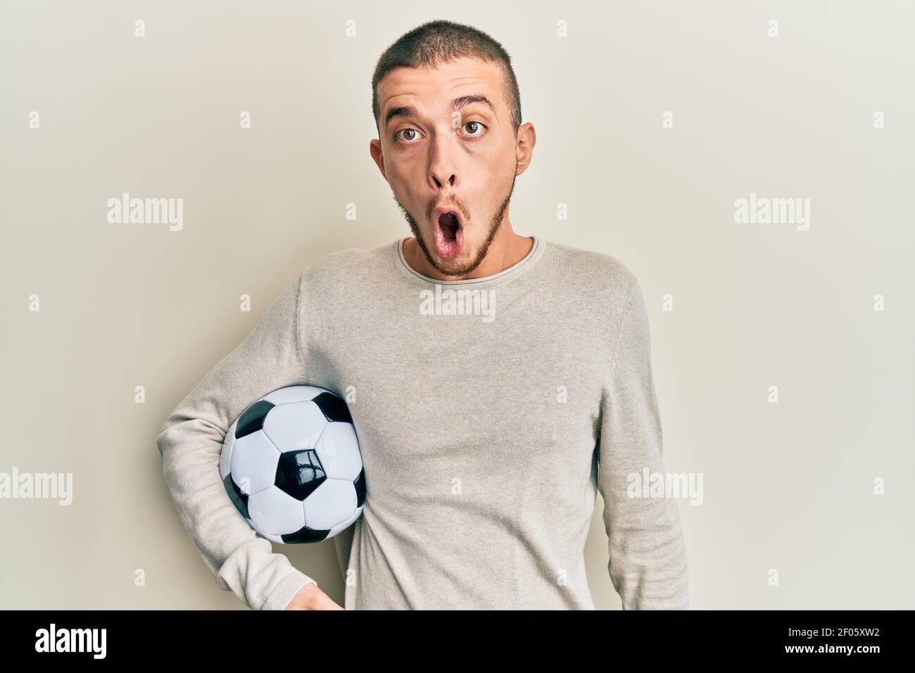 Hispanic young man holding soccer ball scared and amazed with open ...