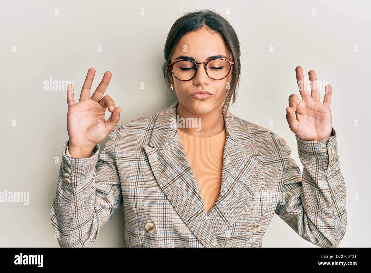 Young brunette woman wearing business jacket and glasses relaxed and ...