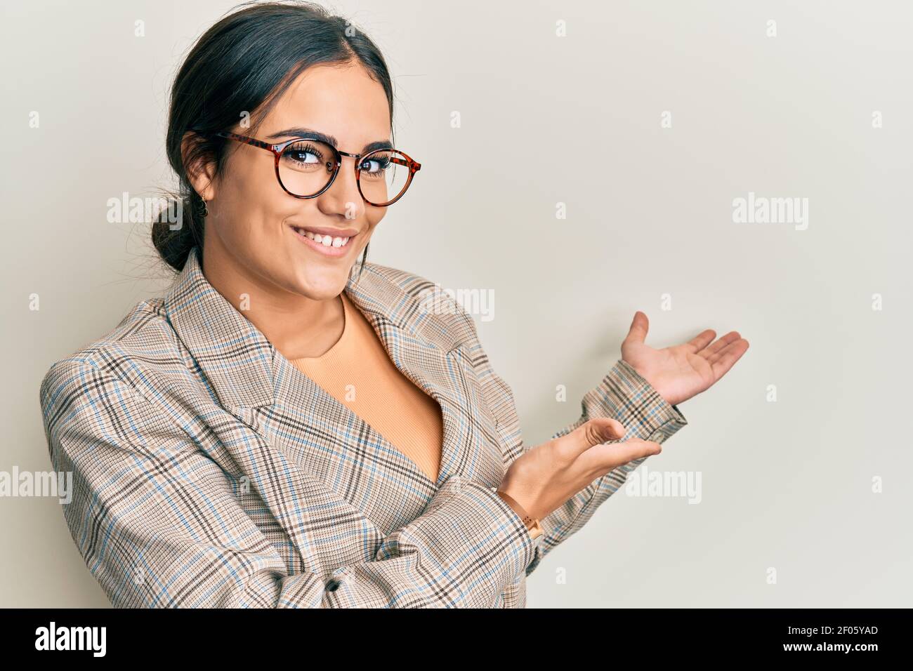 Young brunette woman wearing business jacket and glasses inviting to ...