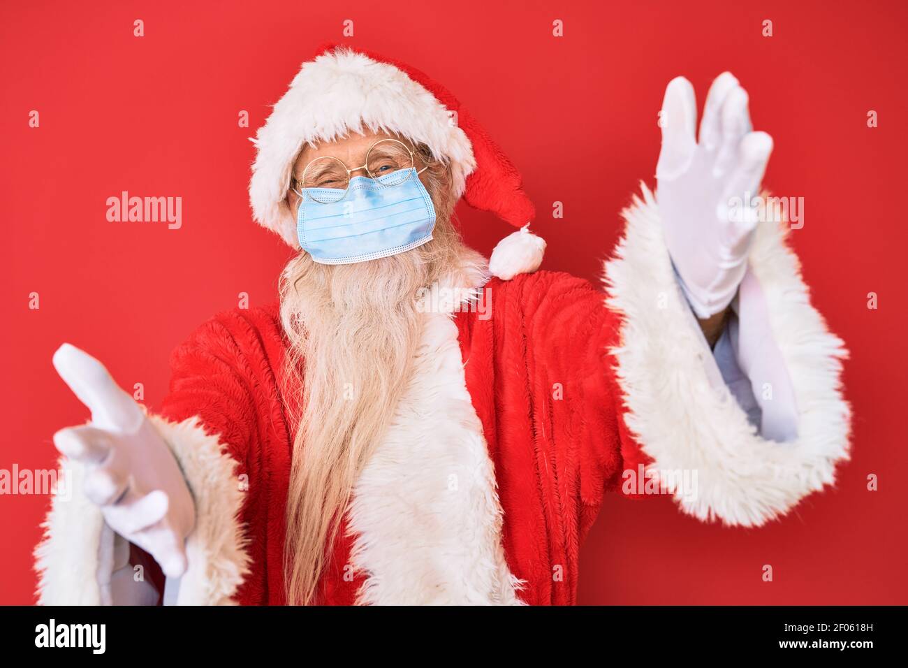 Old senior man wearing santa claus costume wearing safety mask looking ...