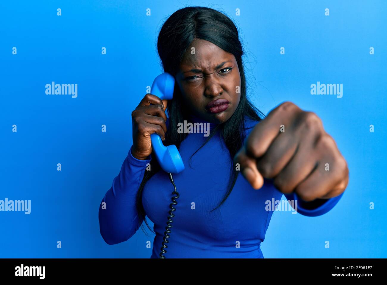 African young woman speaking on vintage telephone annoyed and ...