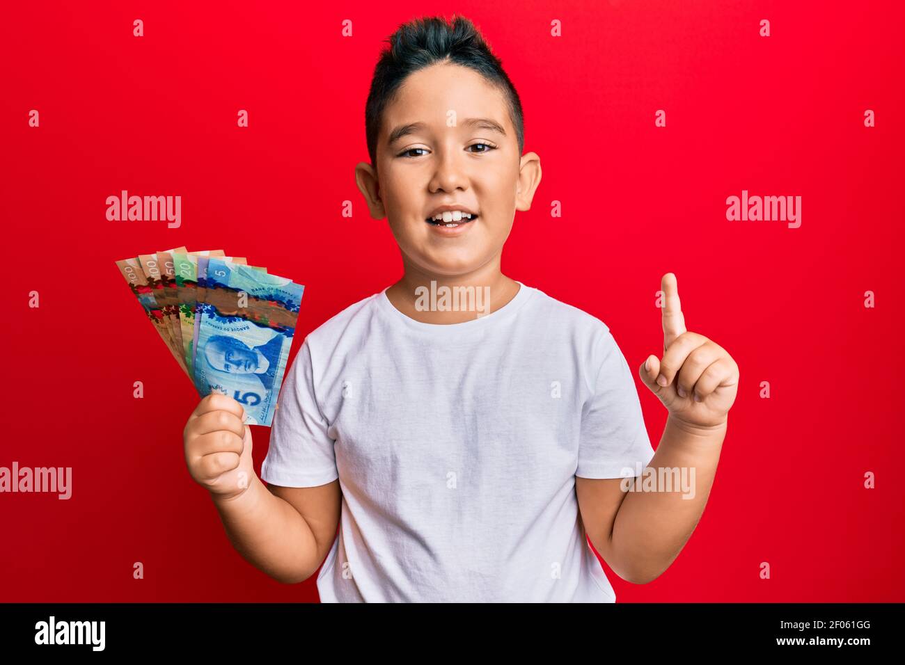 Little boy hispanic kid holding canadian dollars smiling with an idea ...