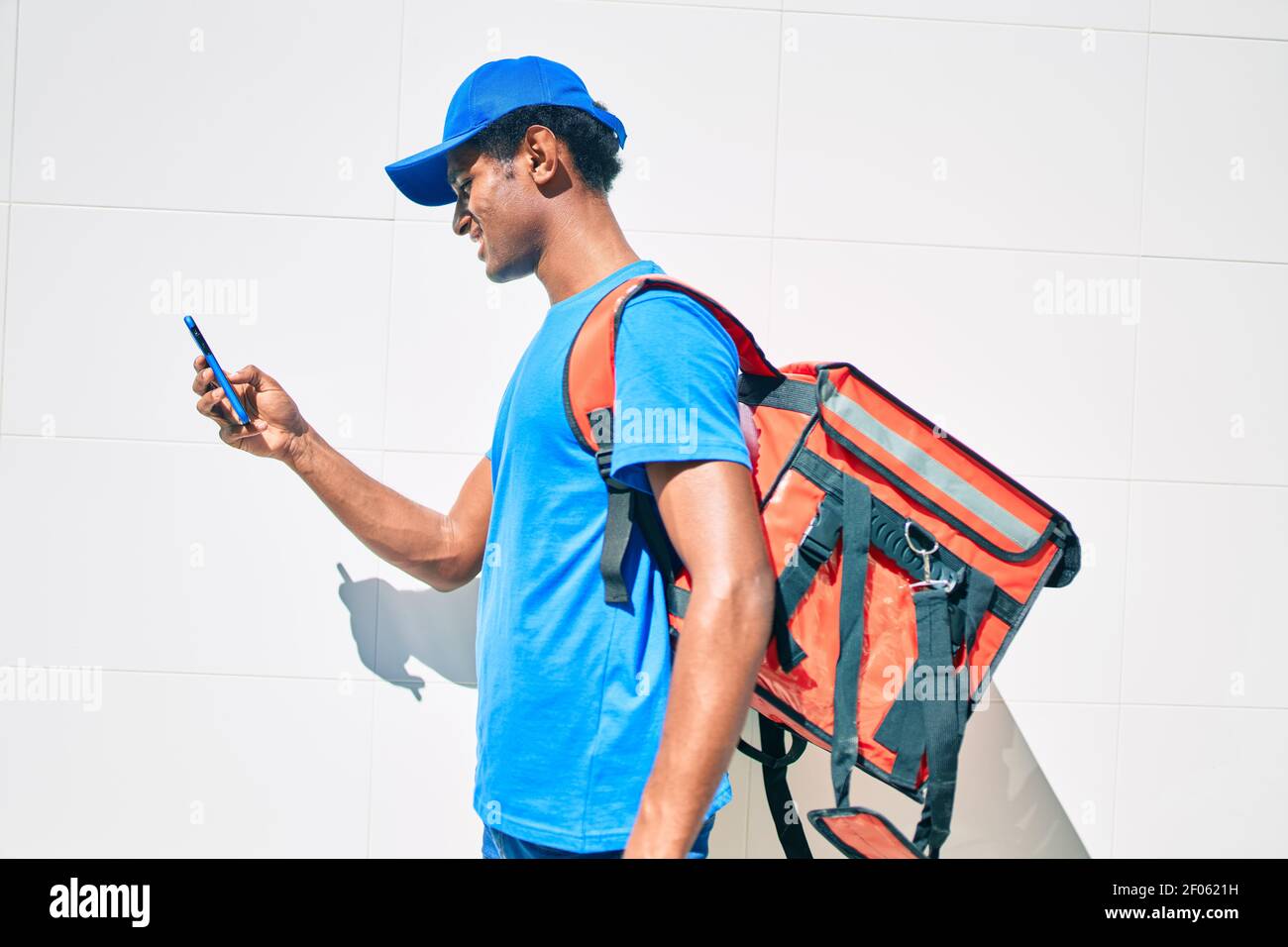 African delivery man wearing courier uniform outdoors using smartphone ...