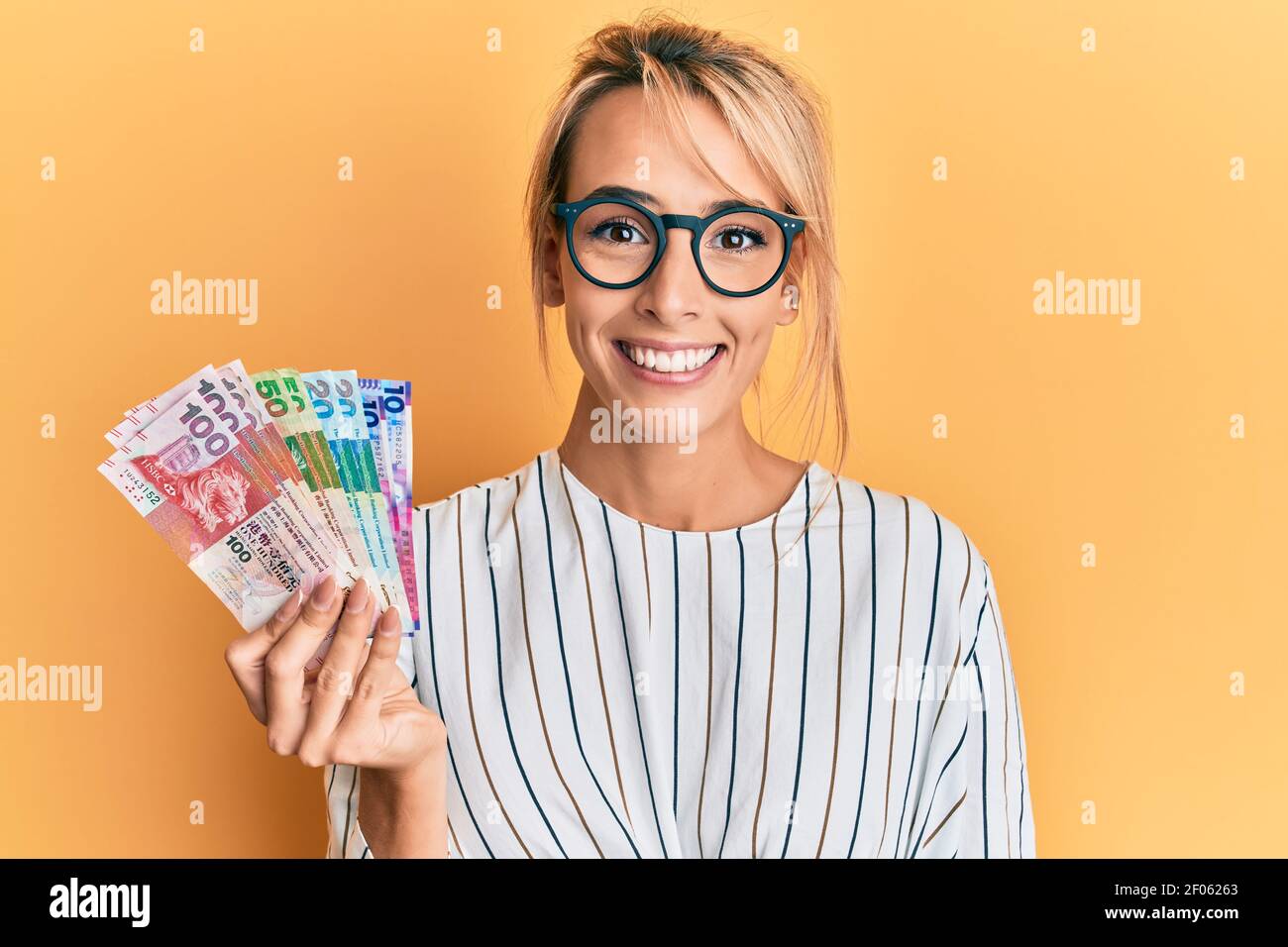 Beautiful blonde woman holding hong kong dollars banknotes looking ...