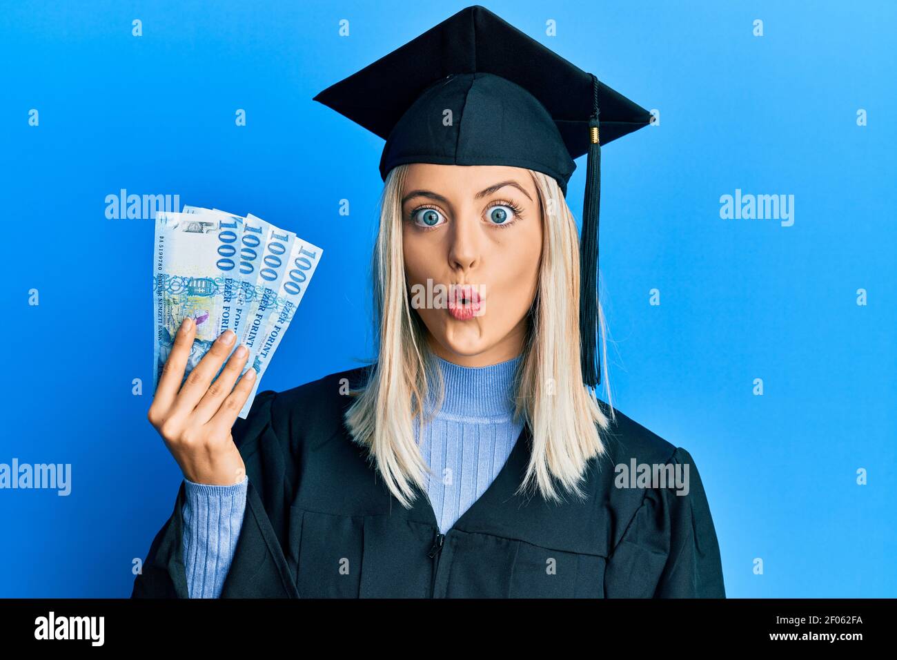 Beautiful blonde woman wearing graduation cap and ceremony robe holding ...