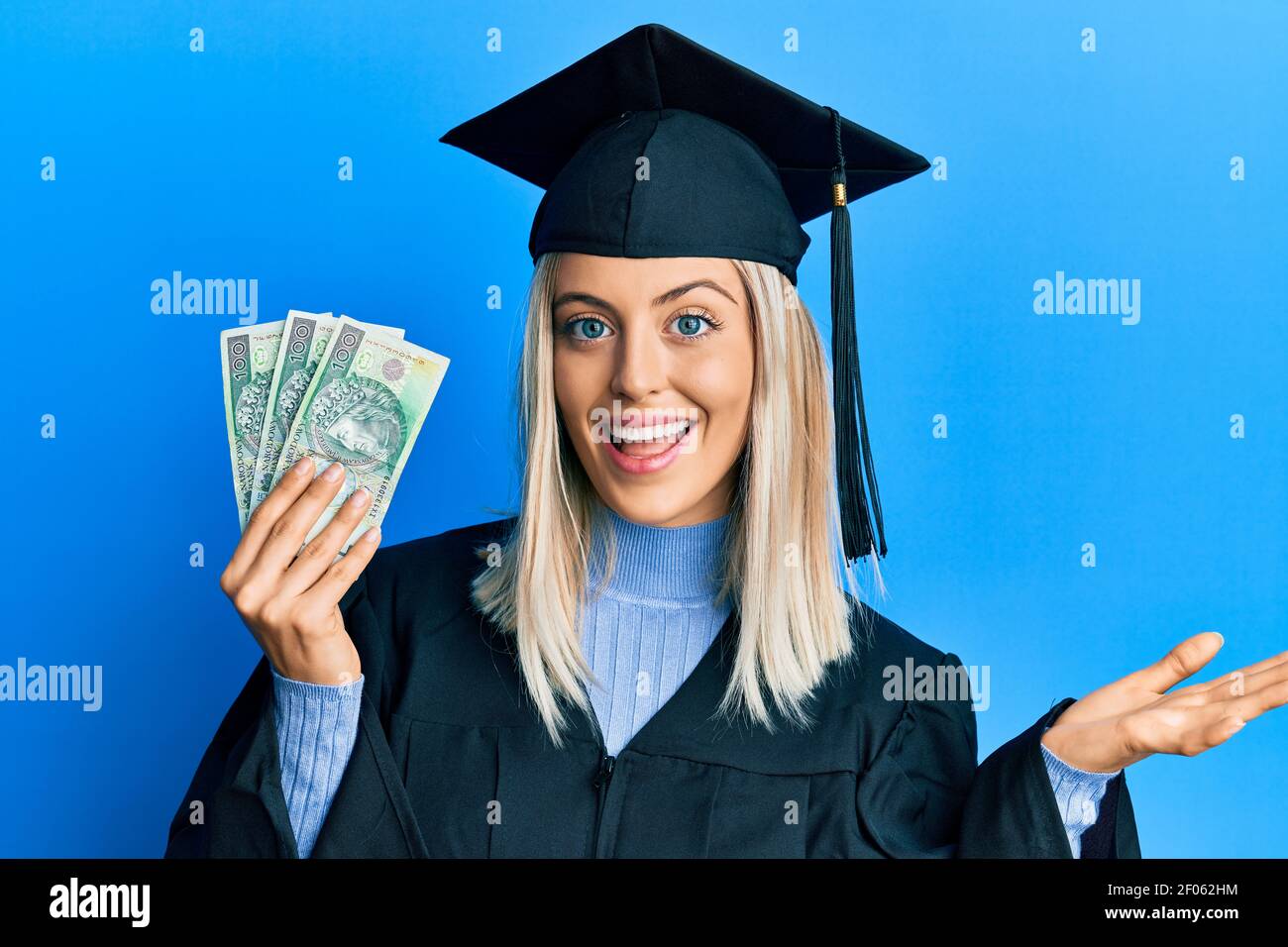 Beautiful blonde woman wearing graduation cap and ceremony robe holding ...