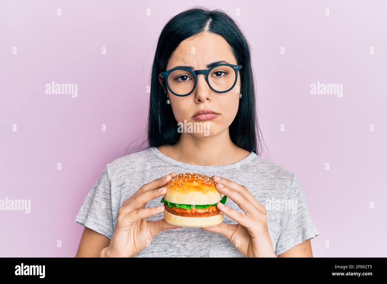 Beautiful young woman eating tasty hamburger depressed and worry for ...