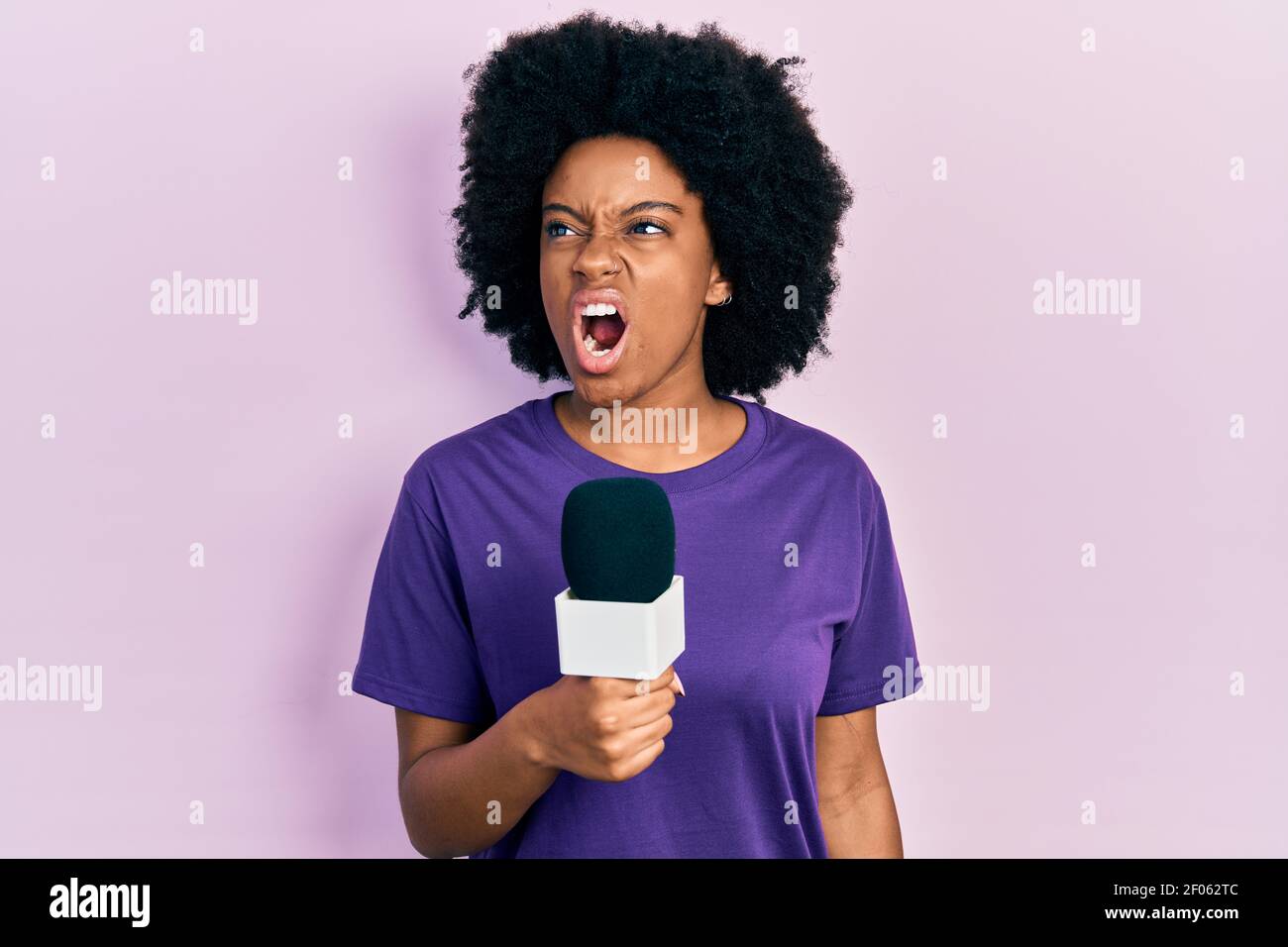 Young african american woman holding reporter microphone angry and mad ...
