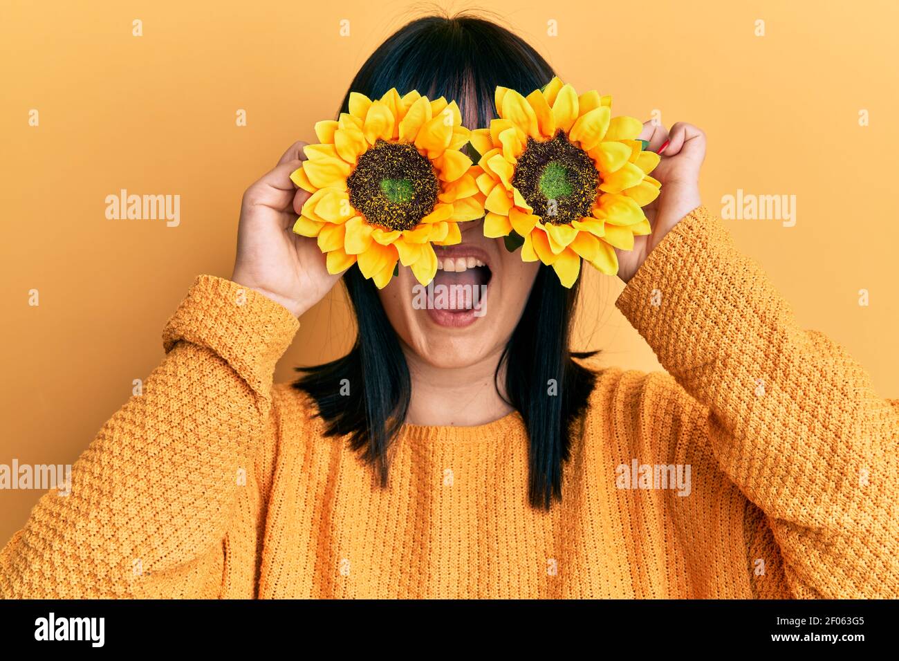 Young hispanic woman holding sunflowers over eyes angry and mad ...