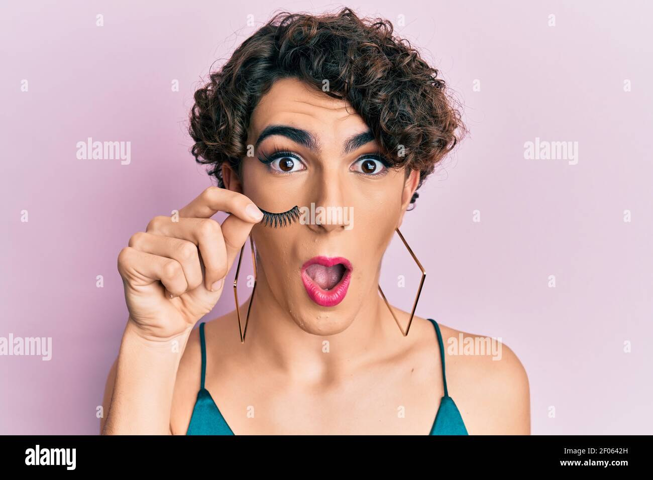 Young man wearing woman make up holding fake lashes scared and amazed ...
