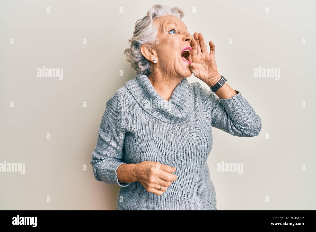 Senior grey-haired woman wearing casual clothes shouting and screaming ...