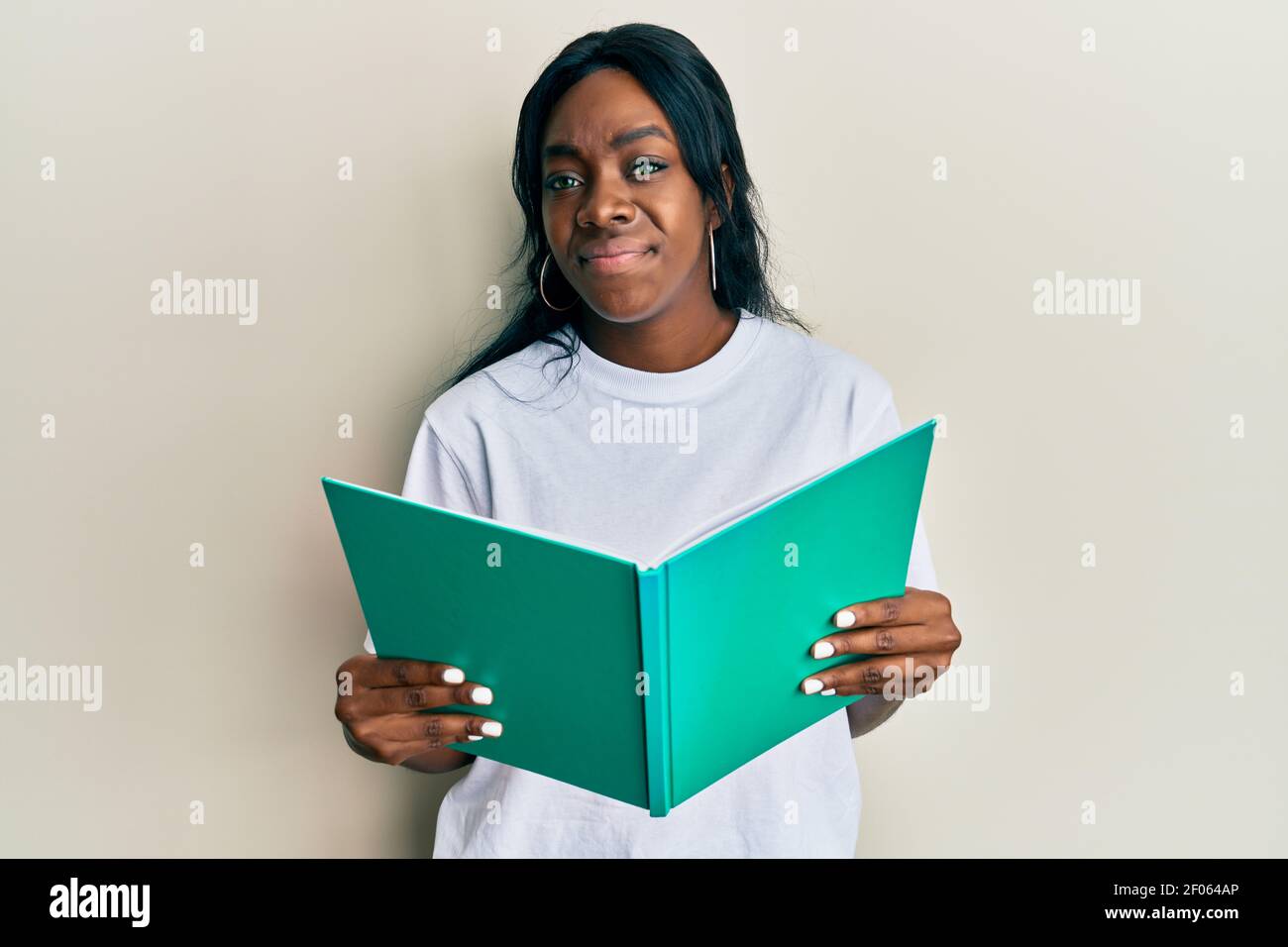 Young african american woman reading book clueless and confused ...