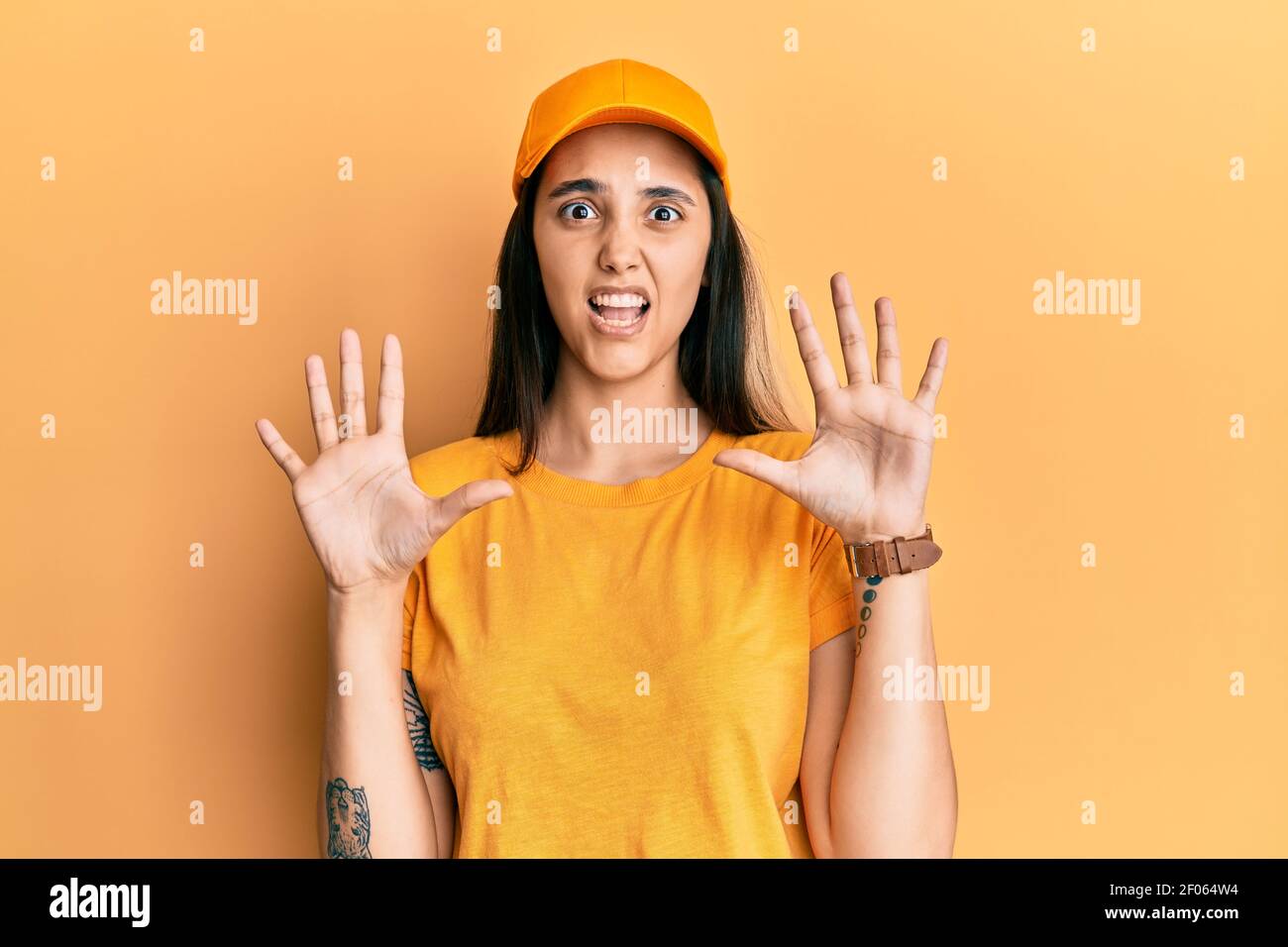Young hispanic woman wearing delivery uniform and cap afraid and ...