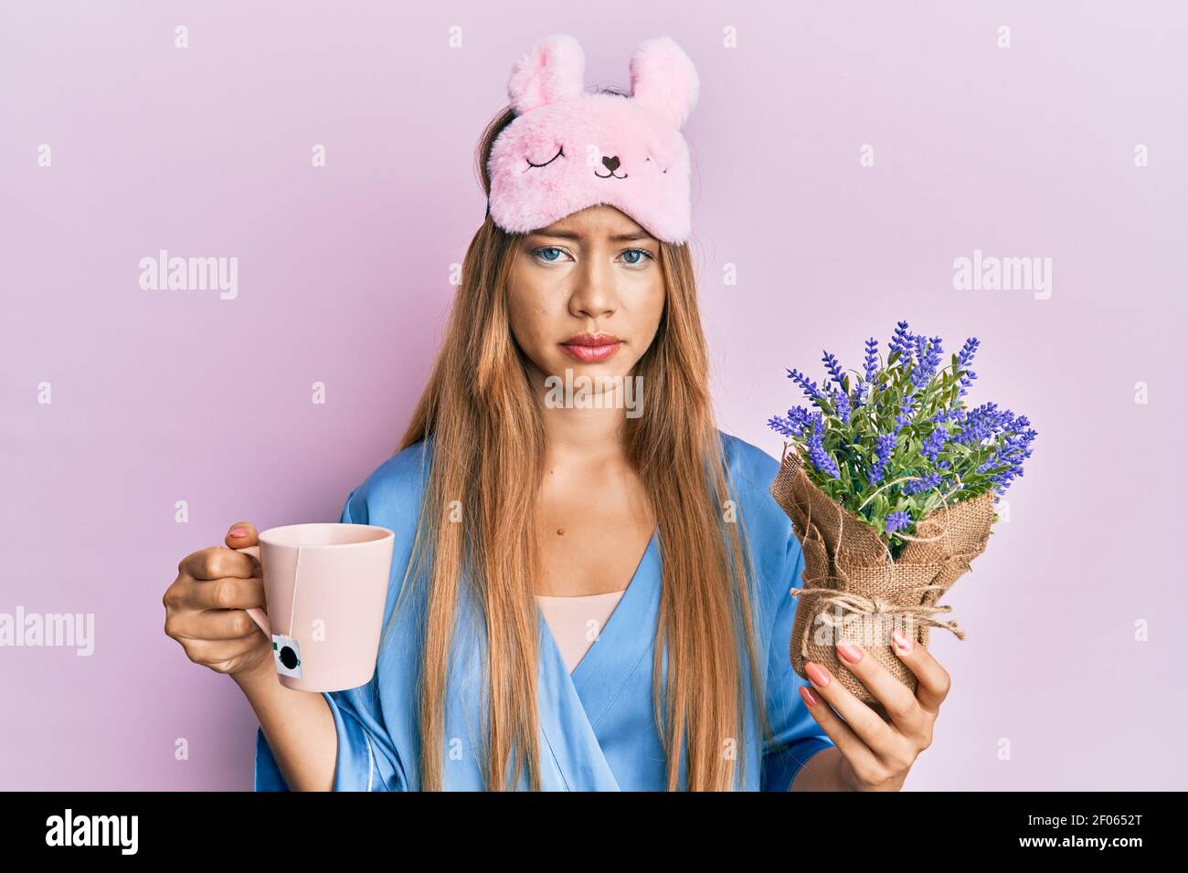Beautiful young blonde woman wearing pajama drinking a cup of infused ...