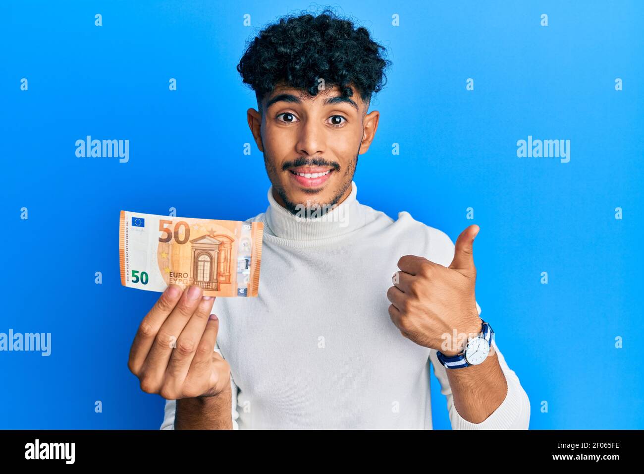 Young arab handsome man holding 50 euro banknote smiling happy and ...