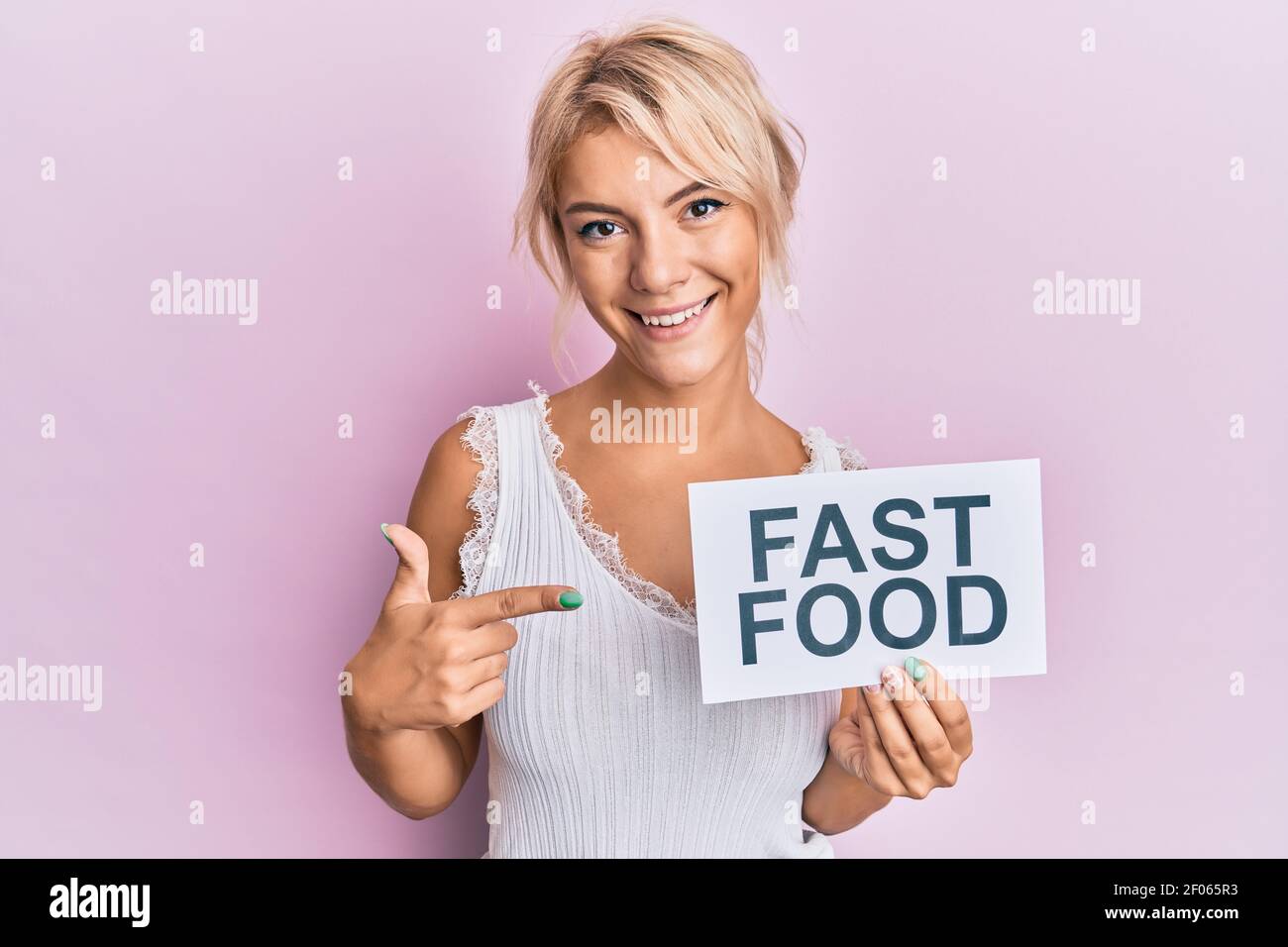 Young blonde girl eating fast food pizza and burger smiling happy ...
