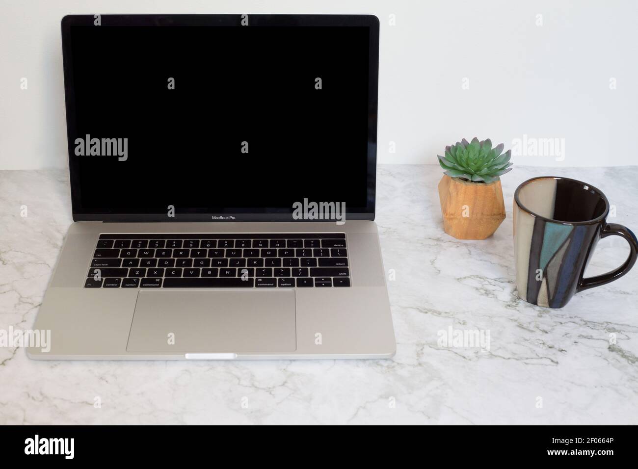 Mac laptop sitting on a marble surface with black screen, cup and small ...