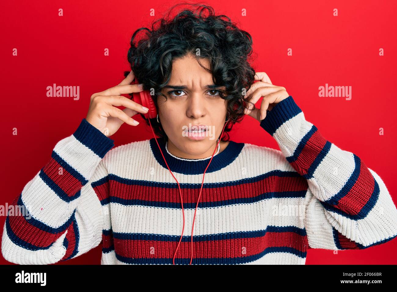Young hispanic woman with curly hair listening to music using ...