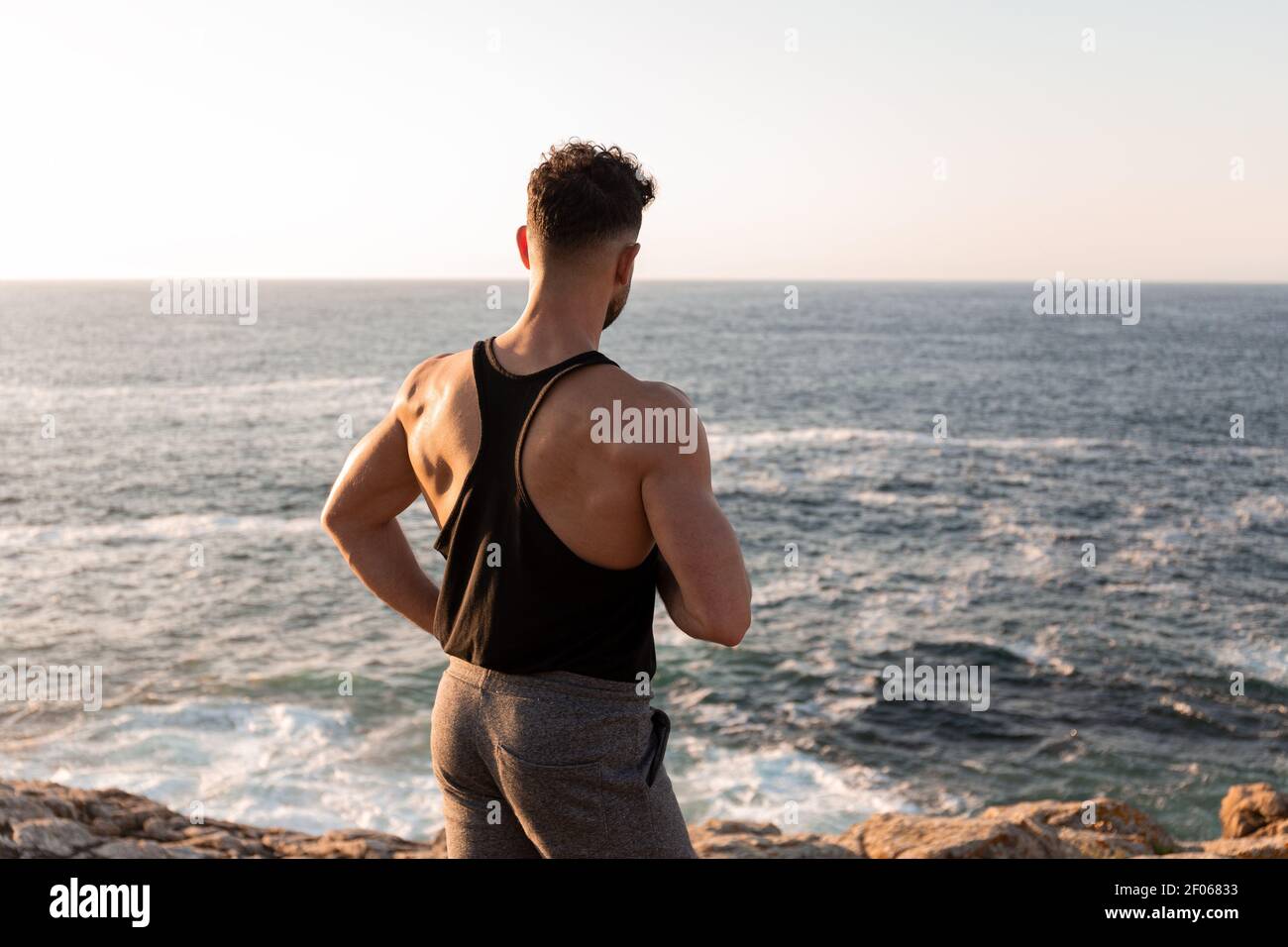 Back view of muscular male athlete in sportswear standing on beach and ...