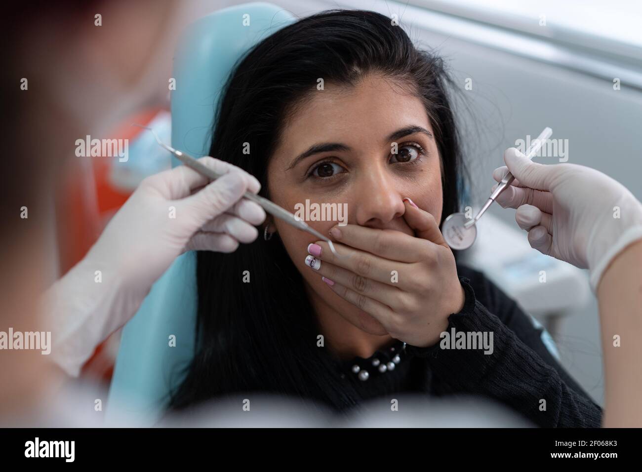 Young frightened female patient looking at camera and covering mouth ...