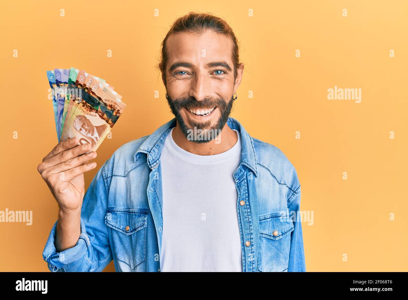 Attractive man with long hair and beard holding canadian dollars ...