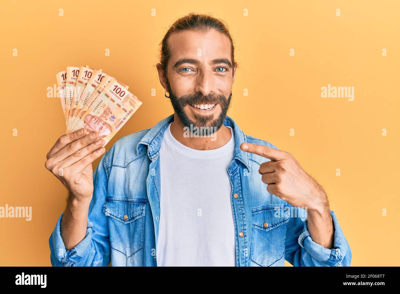 Attractive man with long hair and beard holding 100 mexican pesos ...
