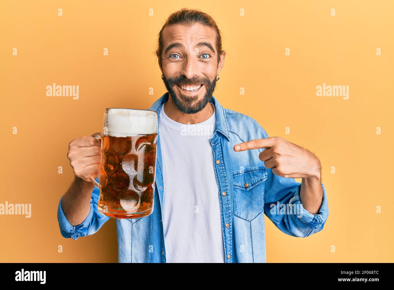 Attractive man with long hair and beard drinking a pint of beer smiling ...