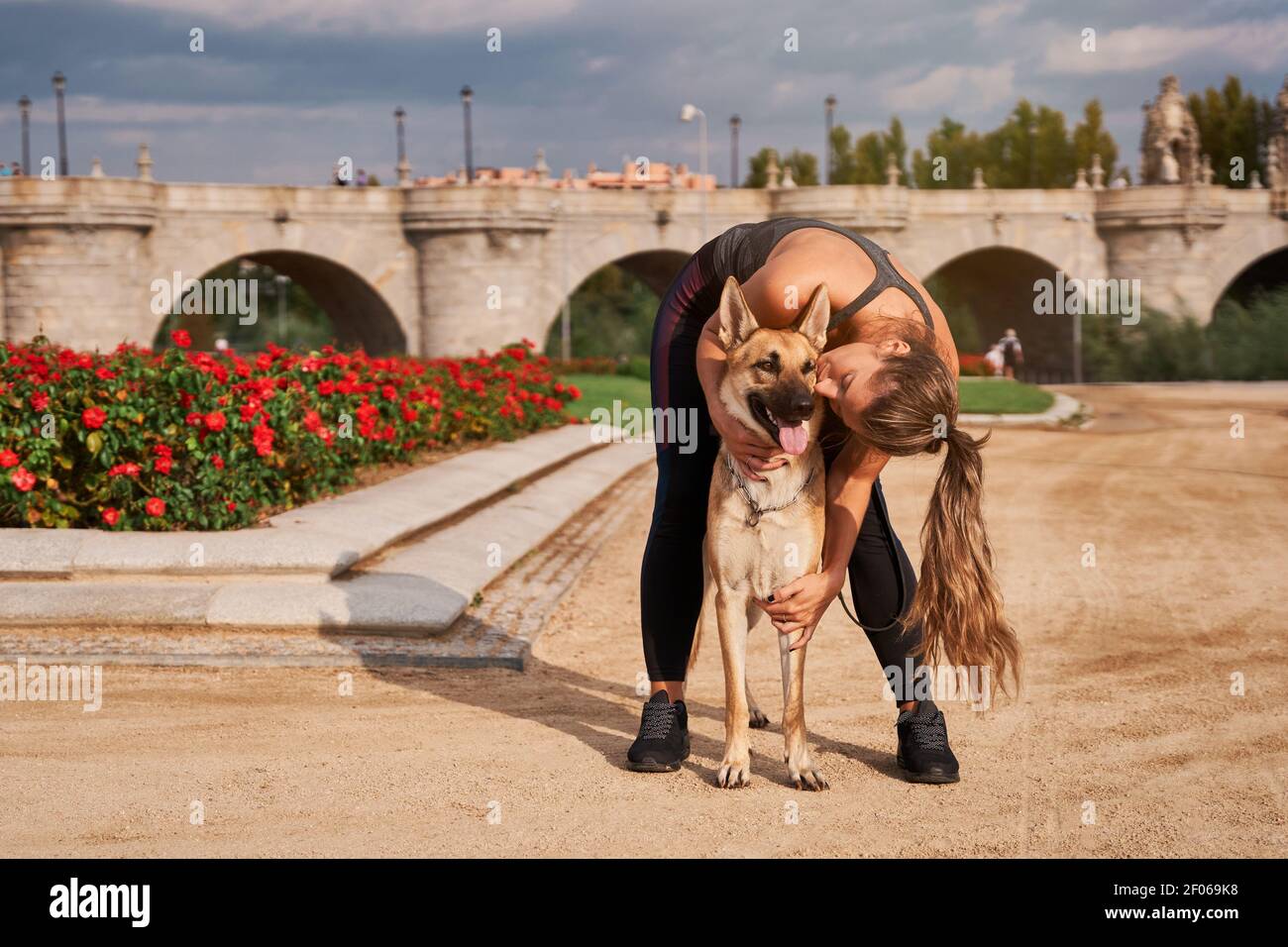Full body of positive female runner kissing German Shepherd dog during ...