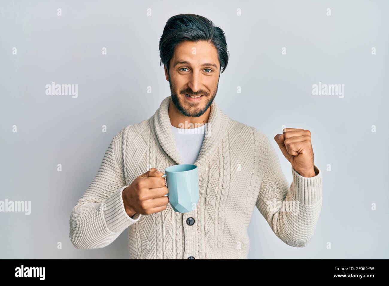 Young hispanic man drinking a cup of coffee screaming proud ...