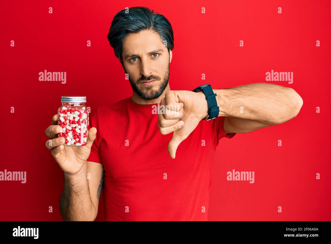 Young hispanic man holding jar of pills with angry face, negative sign ...