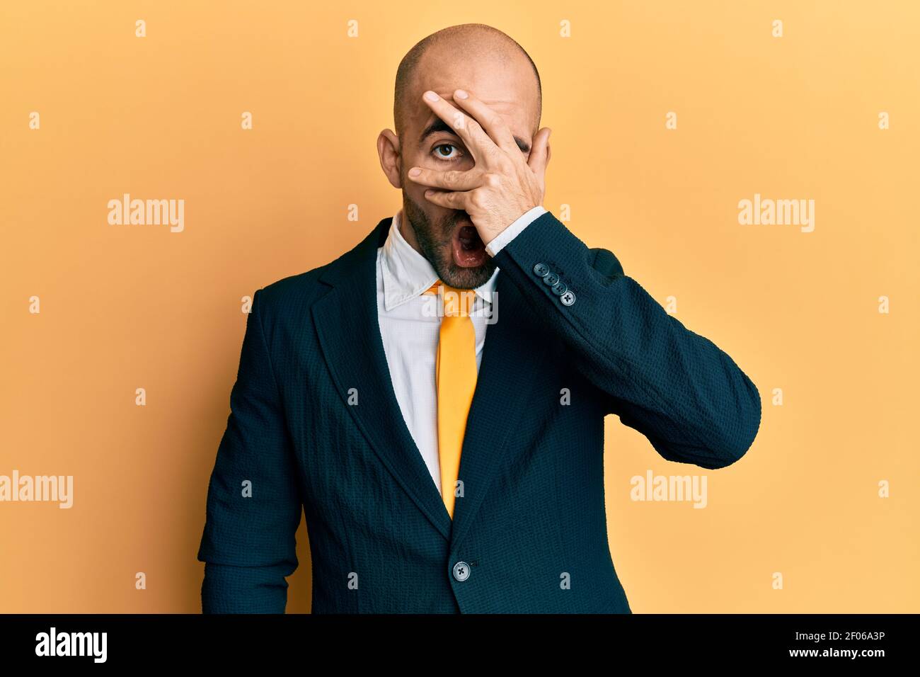 Young hispanic man wearing business suit and tie peeking in shock ...