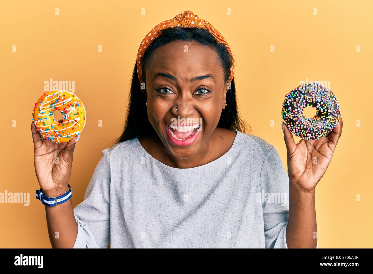 Young african woman holding tasty colorful doughnuts celebrating crazy ...