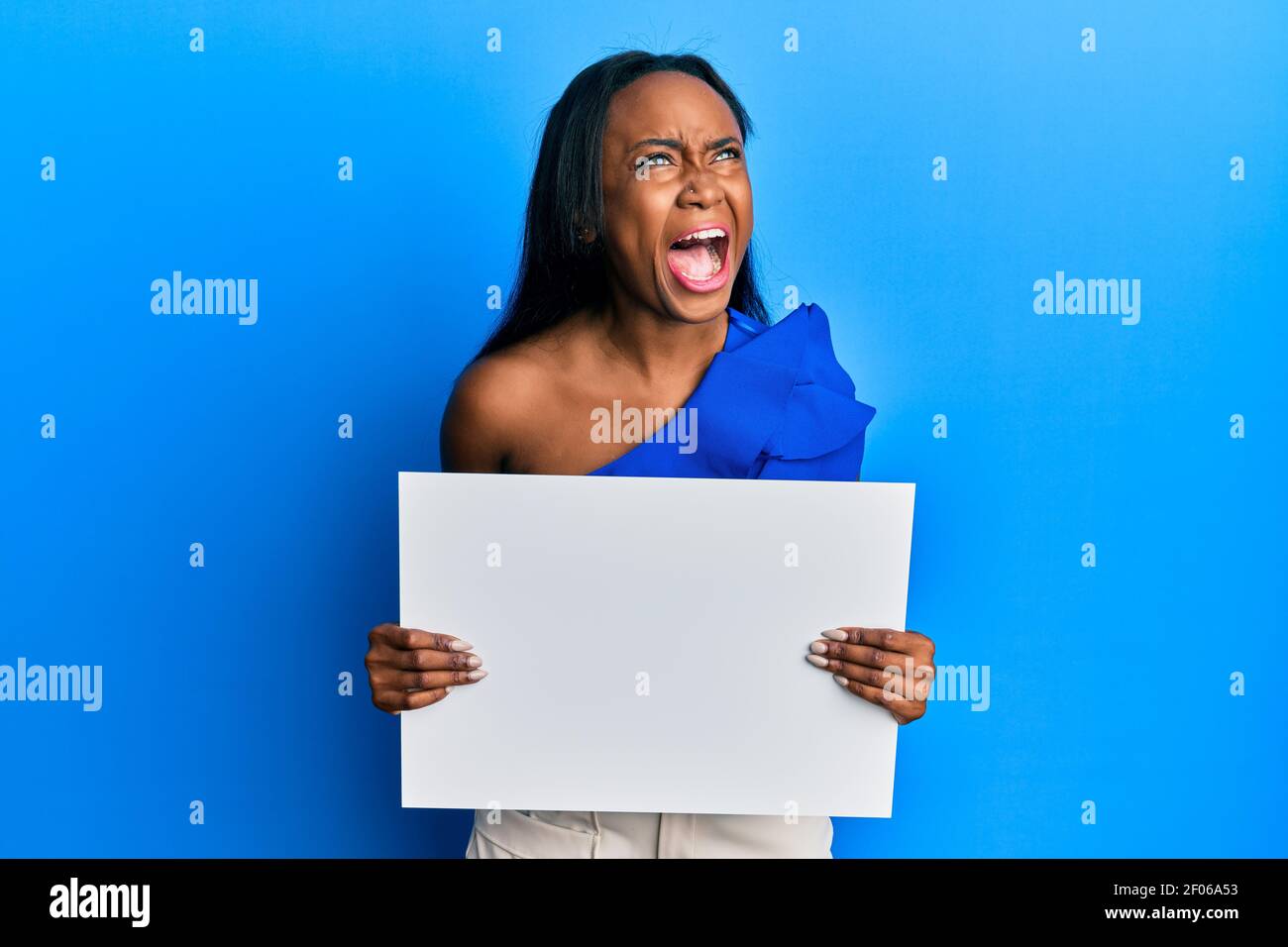 Young african woman holding blank empty banner angry and mad screaming ...