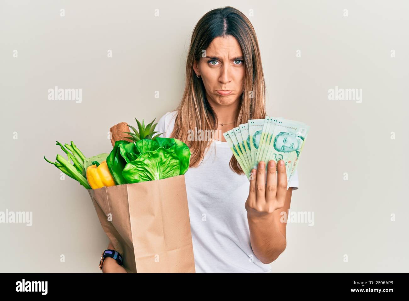 Brunette young woman holding groceries and singapore dollars banknotes ...