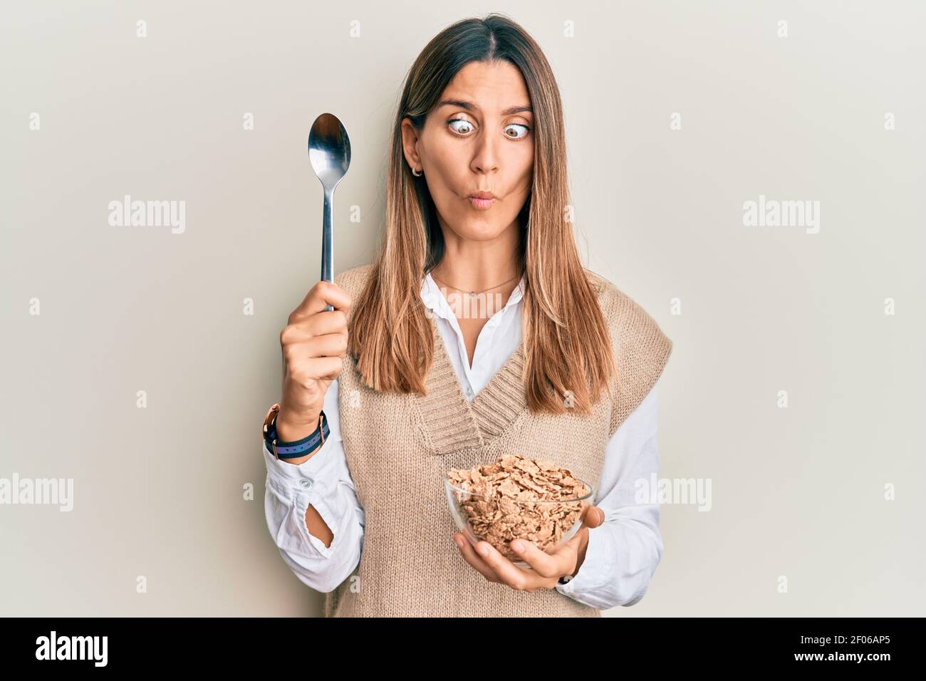 Brunette young woman eating healthy whole grain cereals with spoon ...