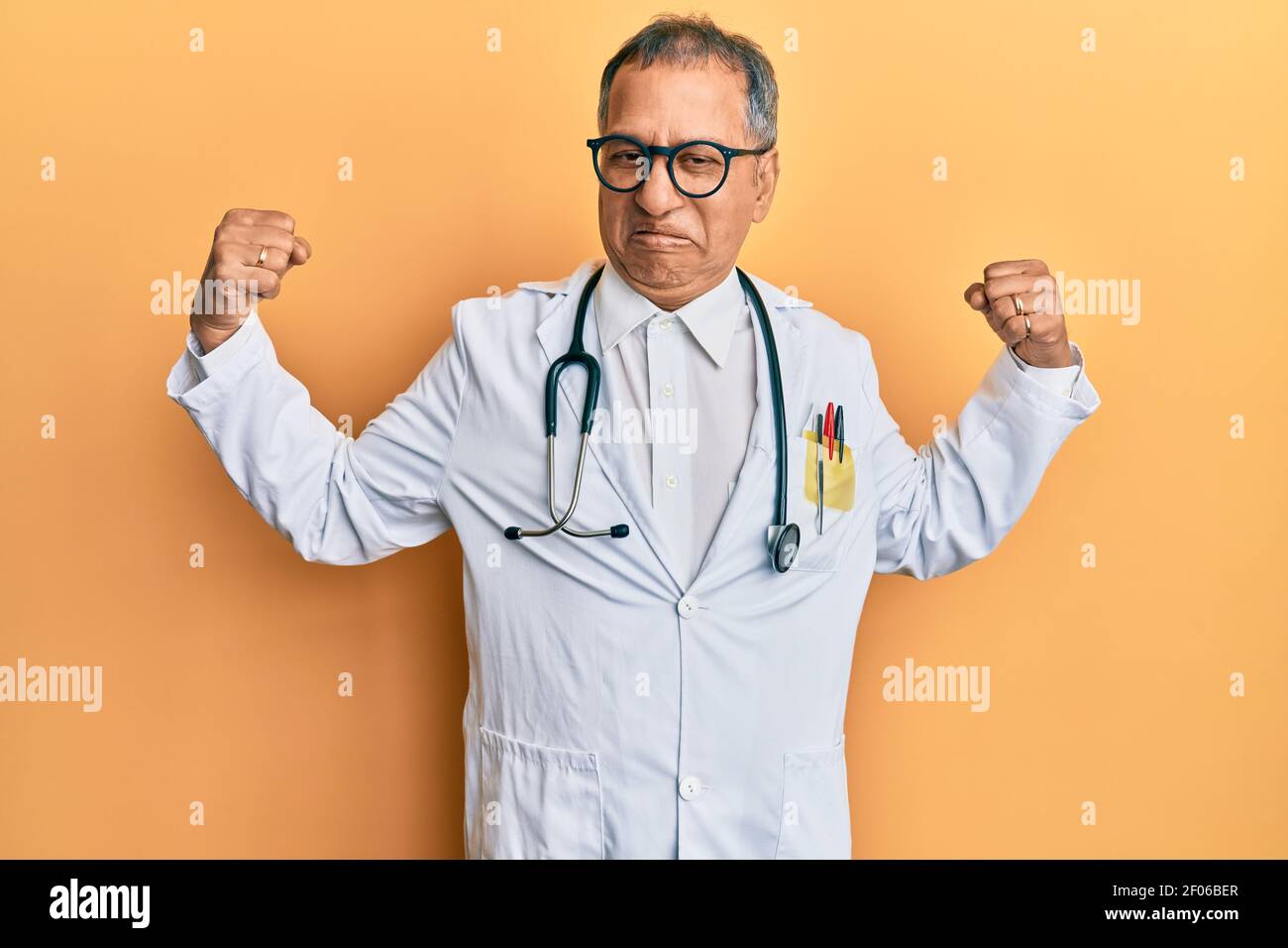 Middle age indian man wearing doctor coat and stethoscope showing arms ...