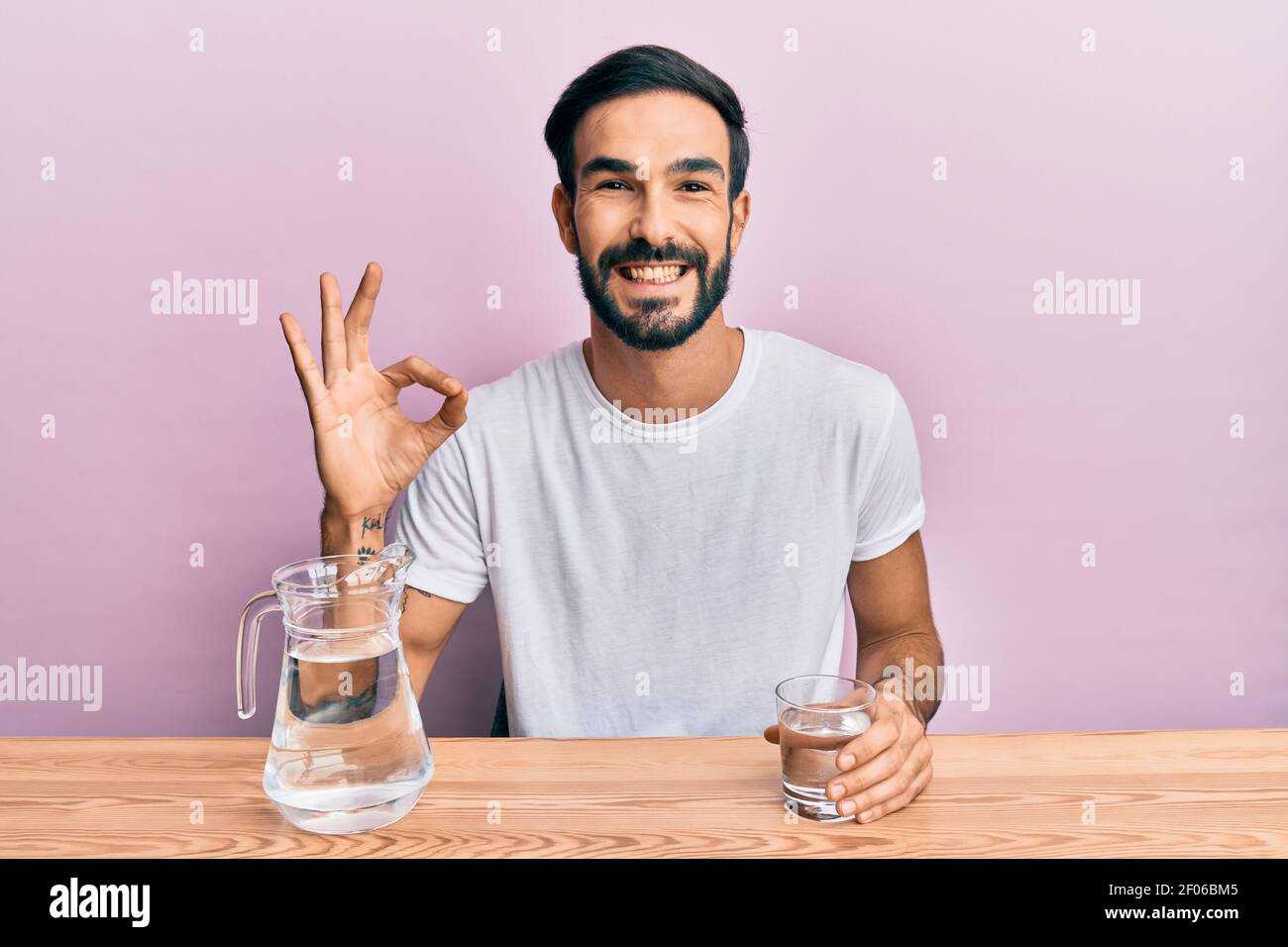 Young hispanic man drinking glass of water sitting on the table doing ...