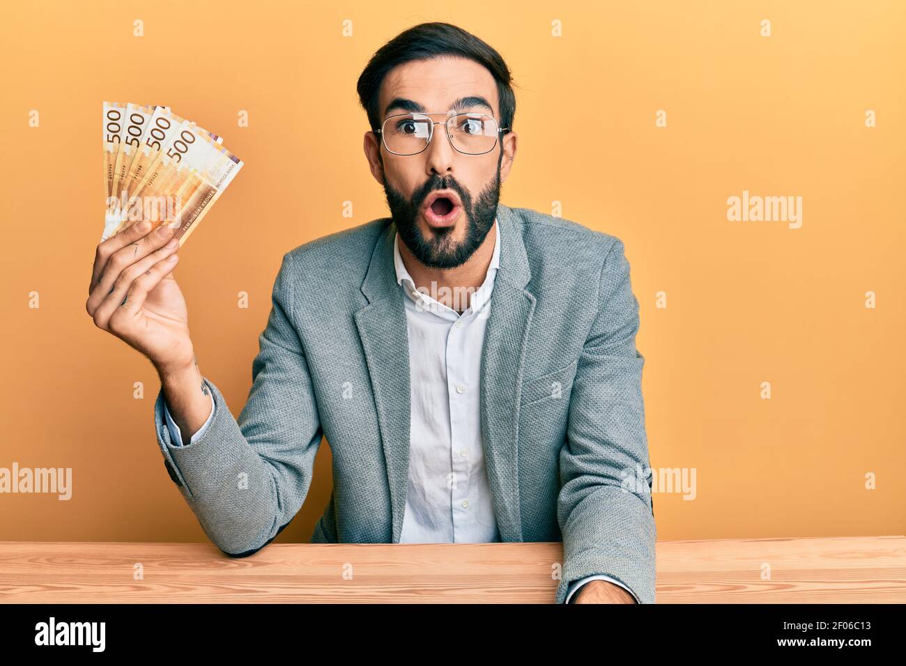 Young hispanic man holding norwegian krone banknotes sitting on the ...