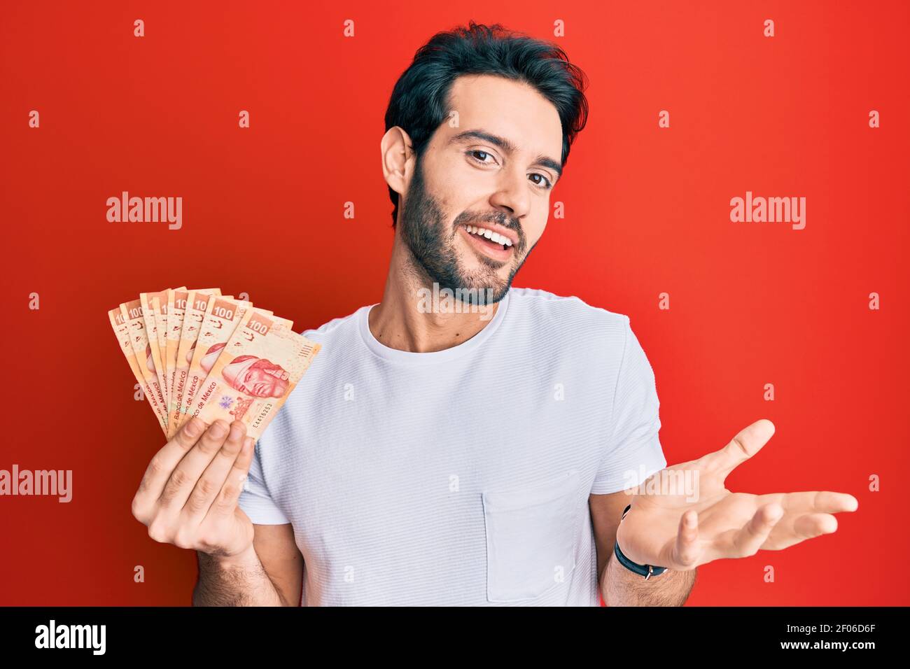 Young hispanic man holding mexican pesos celebrating achievement with ...