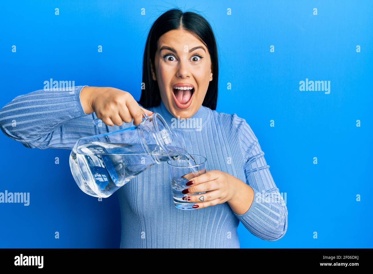 Beautiful brunette woman pouring water in glass celebrating crazy and ...