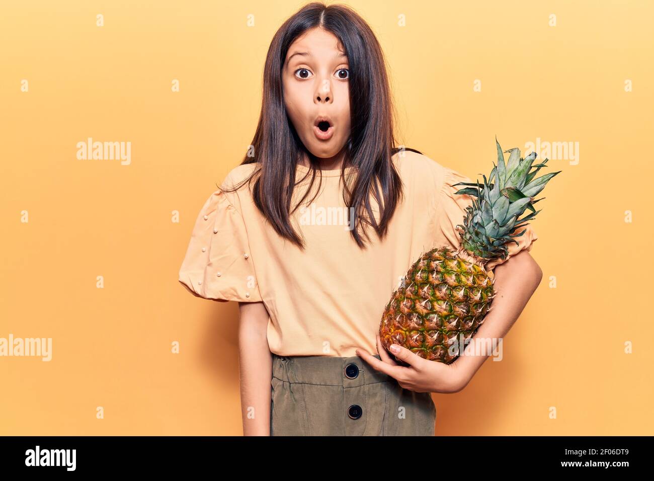 Beautiful child girl holding pineapple scared and amazed with open ...