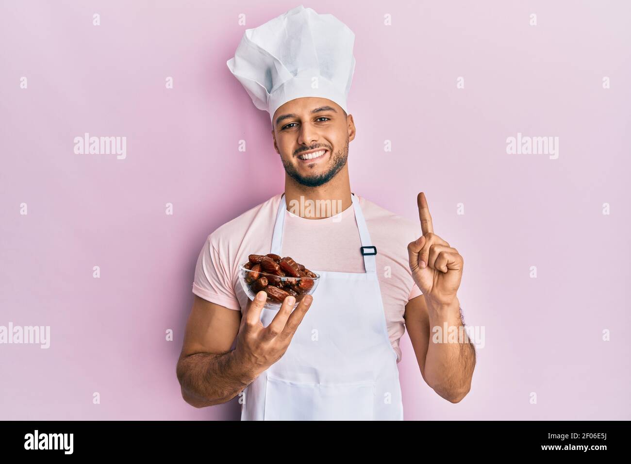 Young arab man wearing professional cook uniform holding bowl with ...