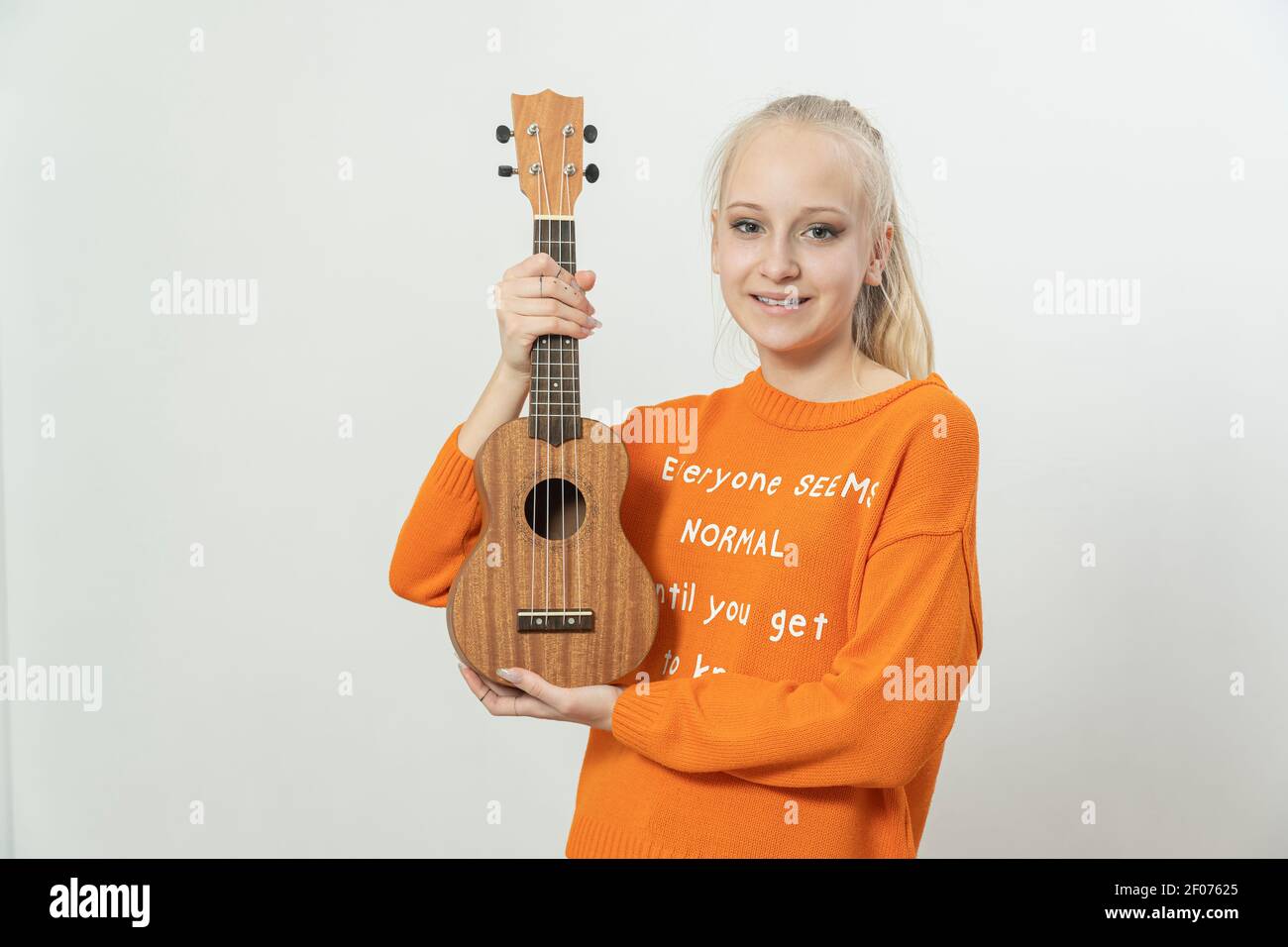 Teenage girl with blond hair keep guitar ukulele on light background ...