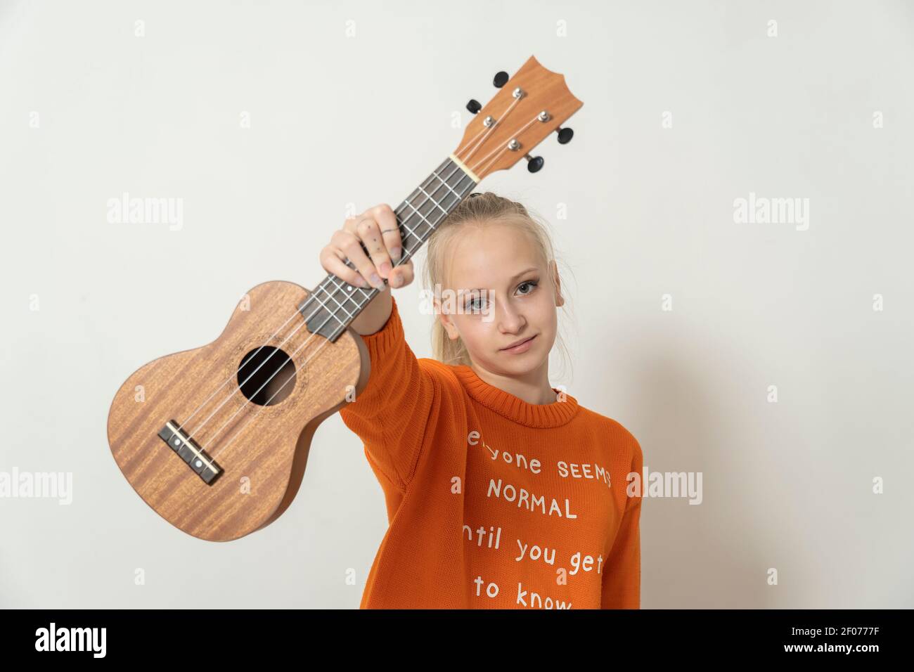 teen girl holding a guitar ukulele and laughing on a light background ...