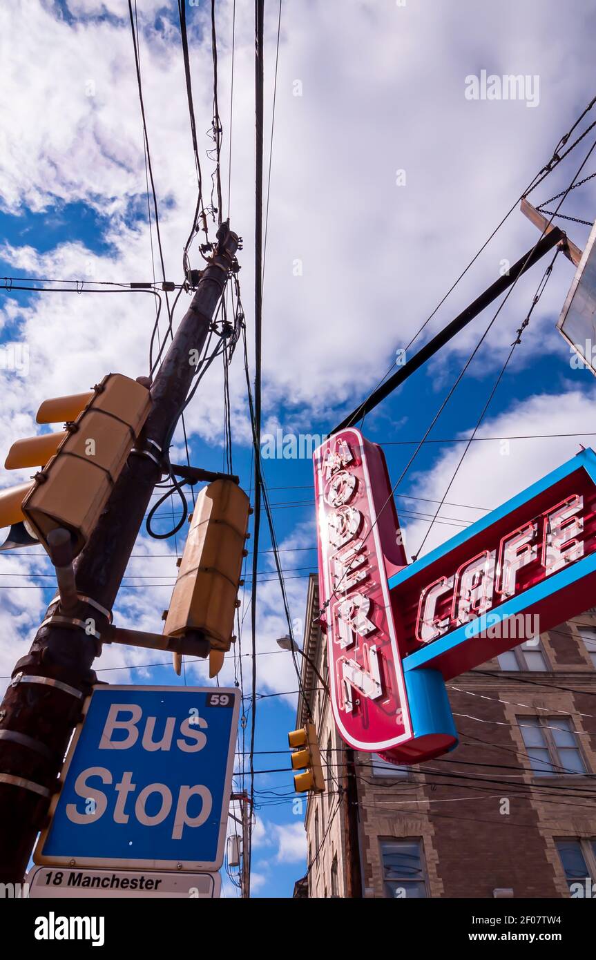 Looking up at a neon sign for the Modern Cafe next to a bus stop sign ...