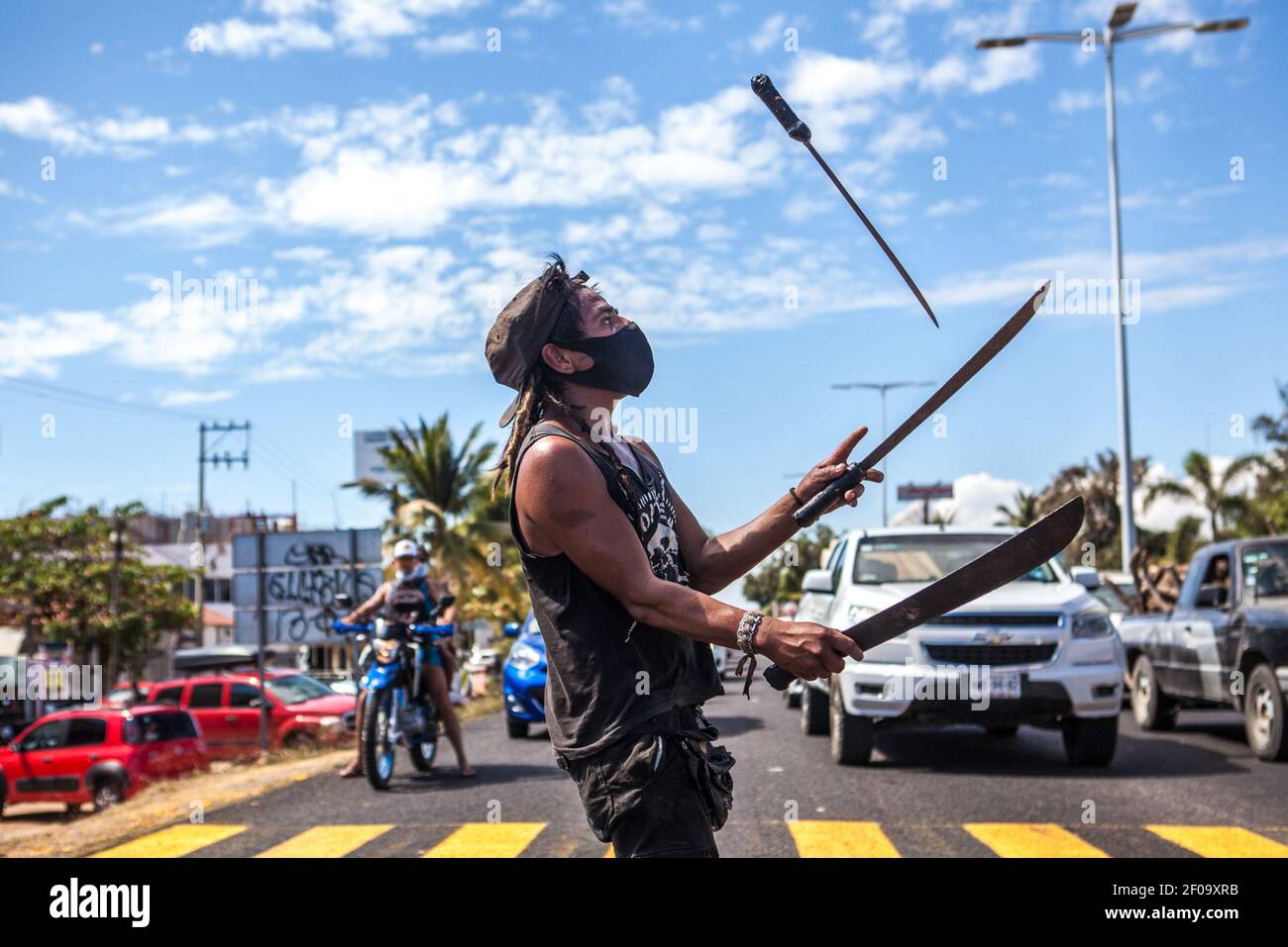 A street juggler wearing a face mask, performs with machetes at the ...