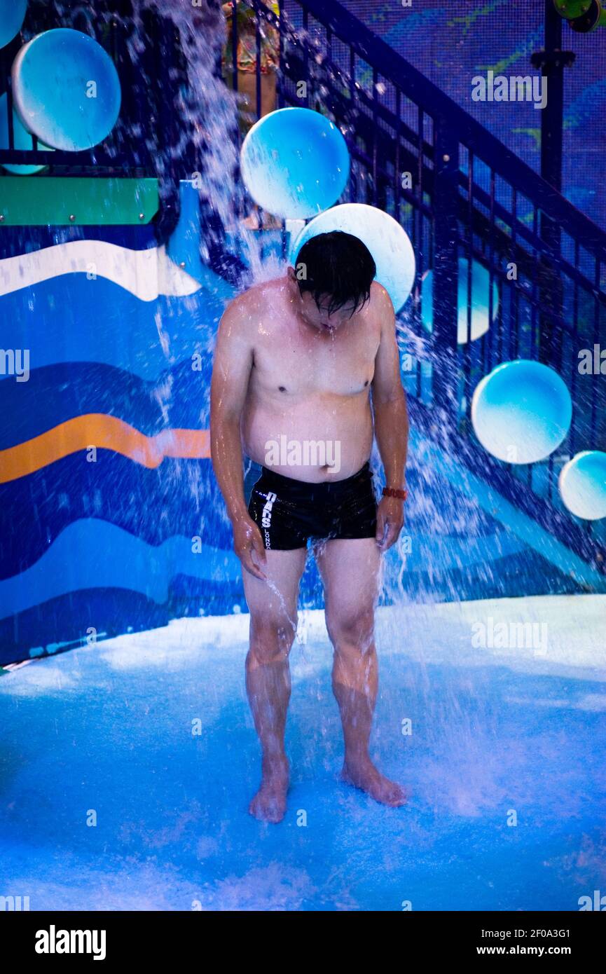 A man underneath a water fountain at the Magic Water Park in Beijing ...