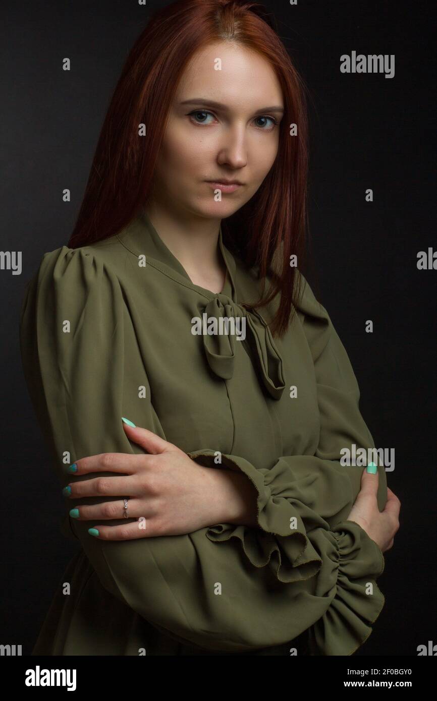 ginger young woman on black background in a green shirt. crossed her ...
